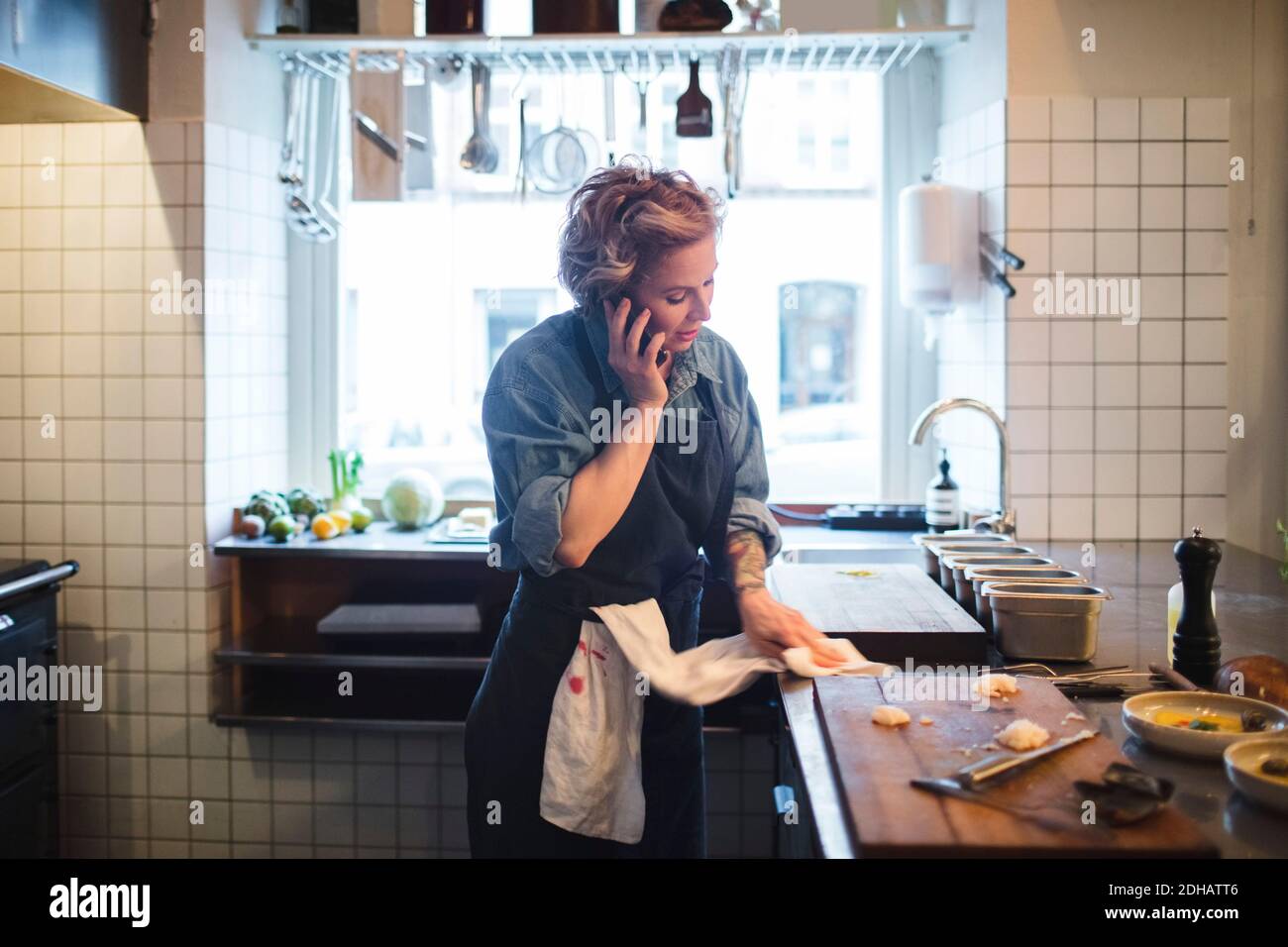 Female chef talking on mobile phone while cleaning kitchen counter in ...