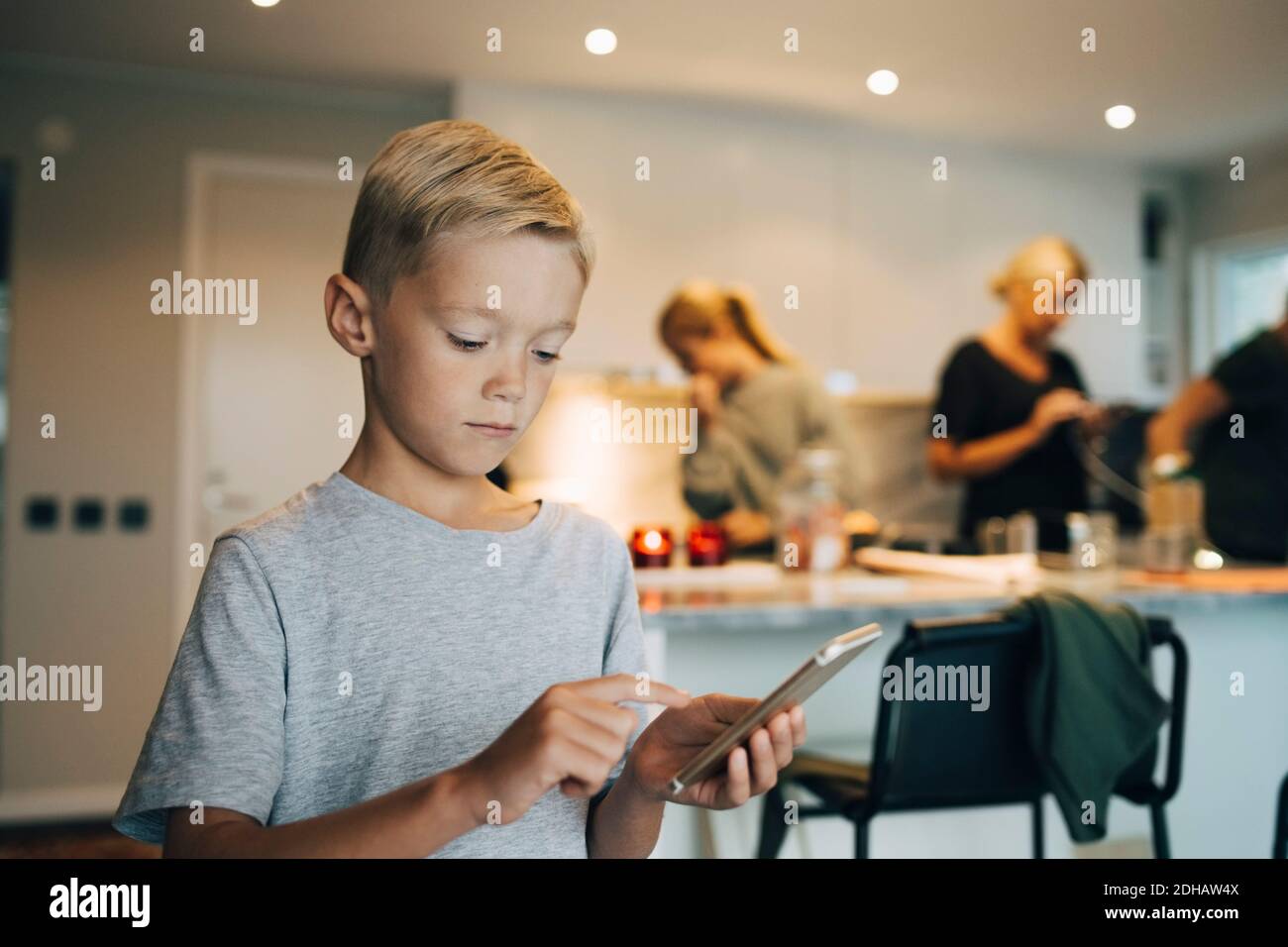 Boy using mobile phone while standing against family in background ...