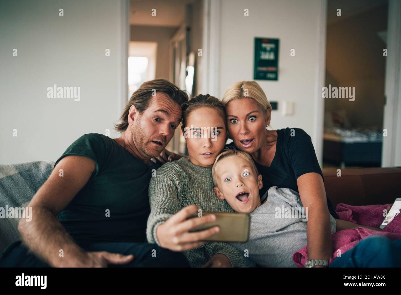 Shocked family taking selfie through smart phone while sitting on sofa ...
