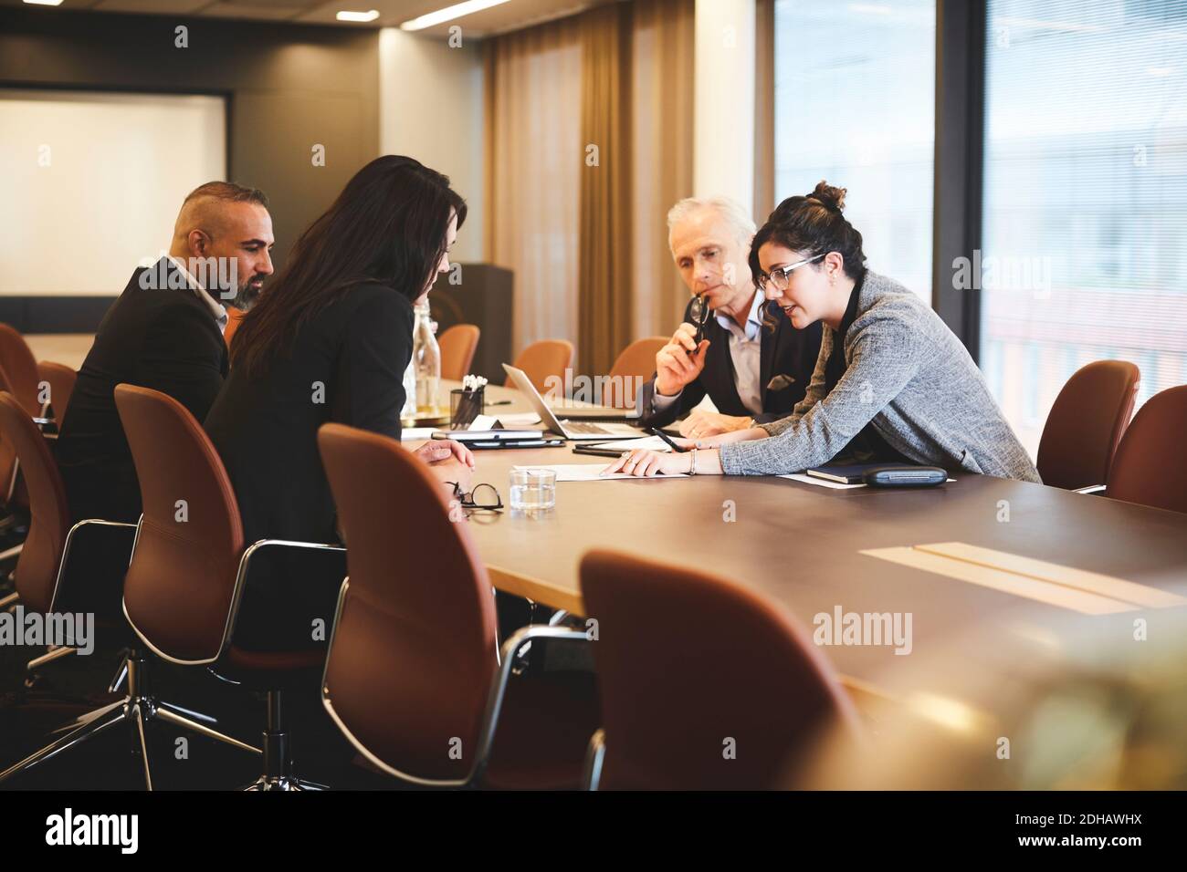 Male and female lawyers discussing over document at conference table in ...