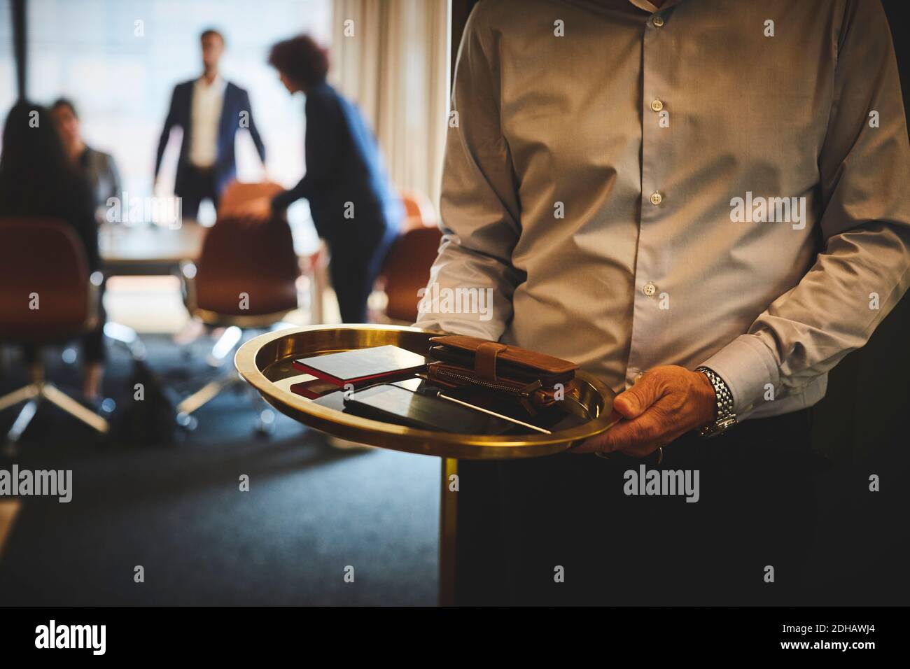 Midsection of professional holding mobile phones in tray at board room ...