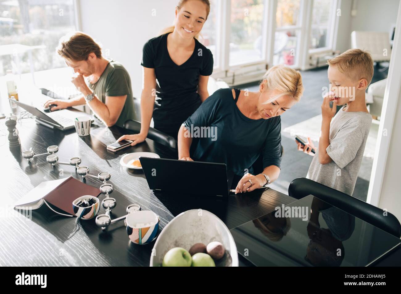 High angle view of family using technologies at dining table in room ...