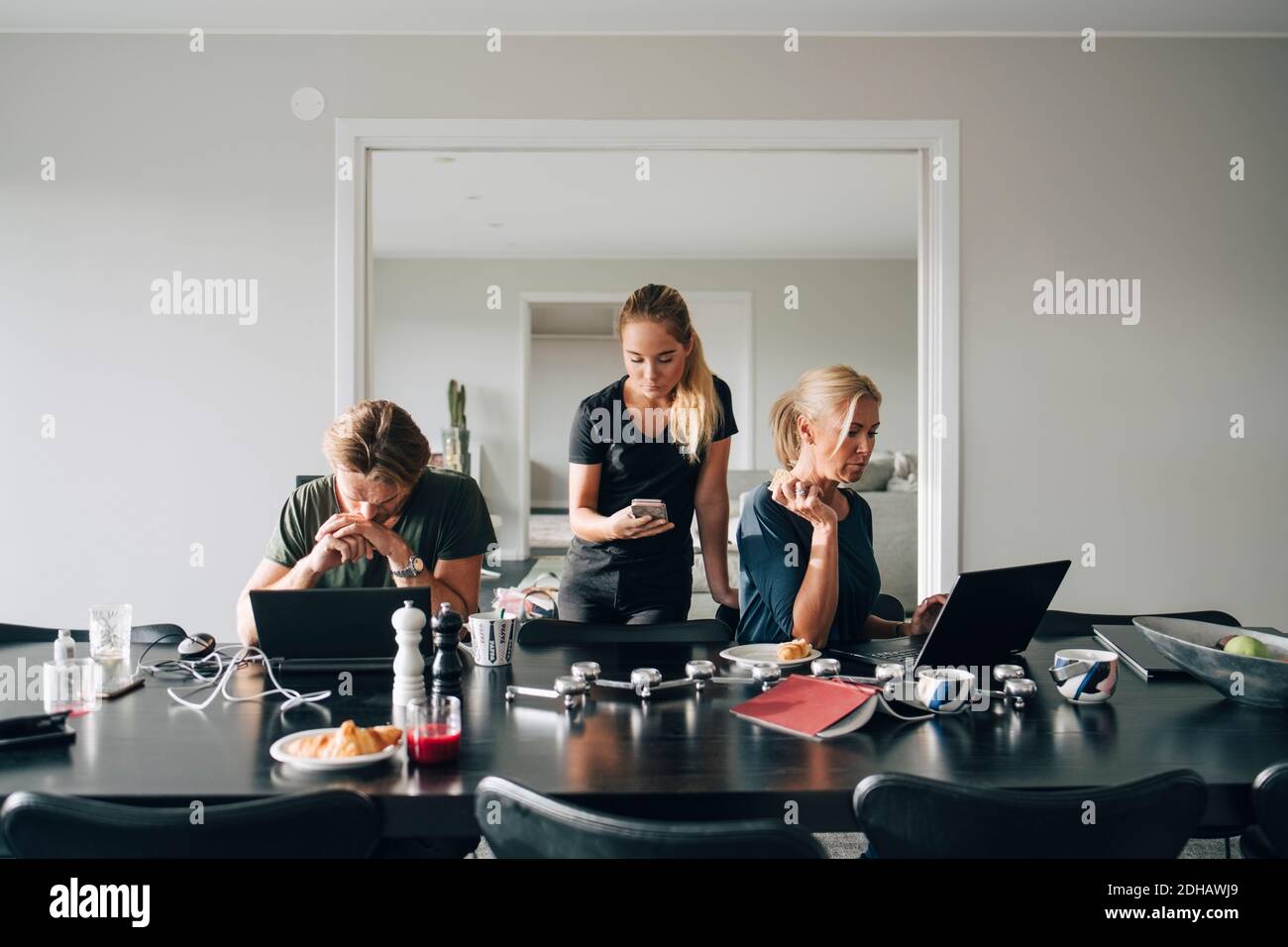 Family using technologies at dining table in room Stock Photo - Alamy