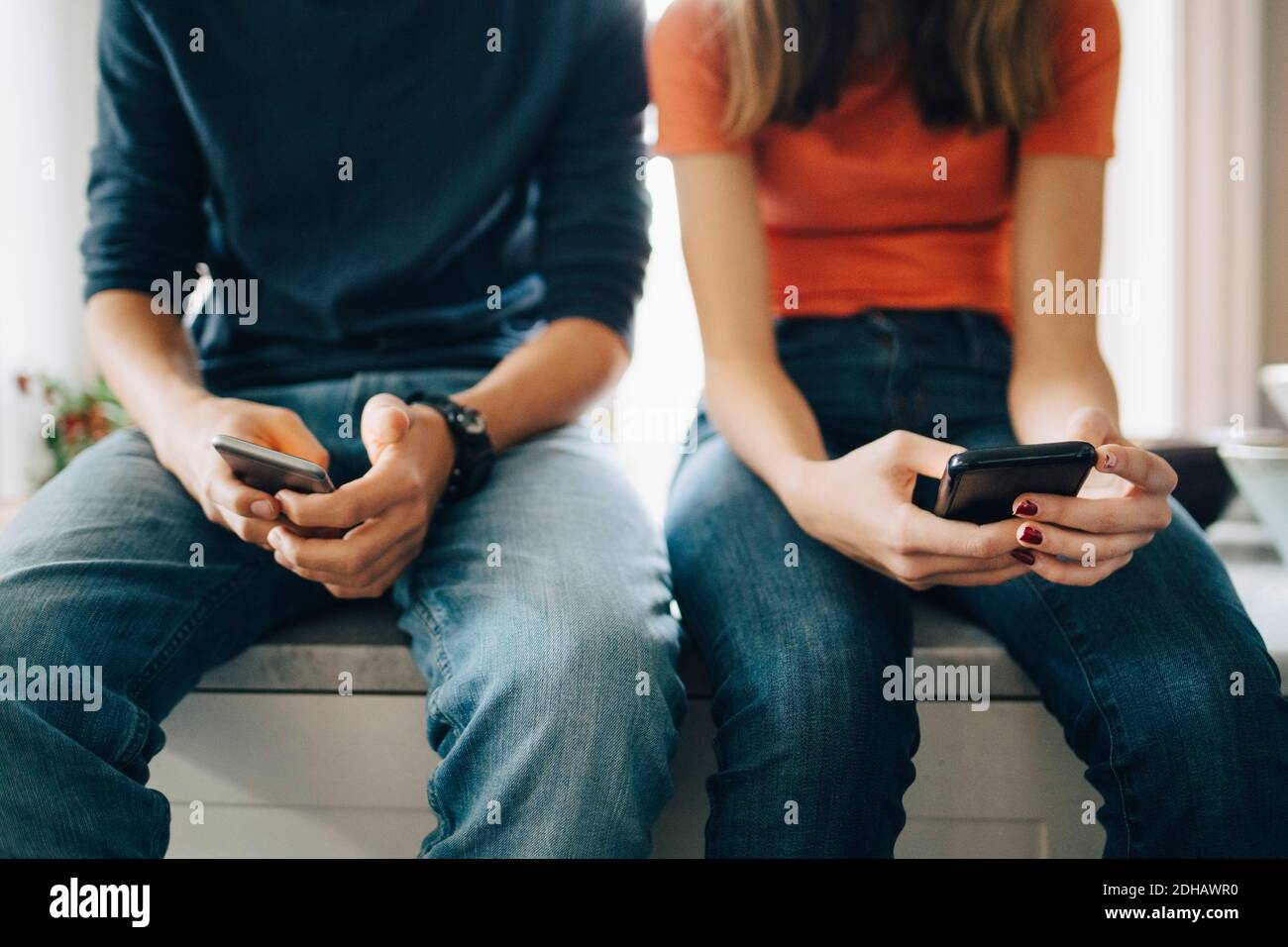 Midsection of male and female friends using mobile phones while sitting ...