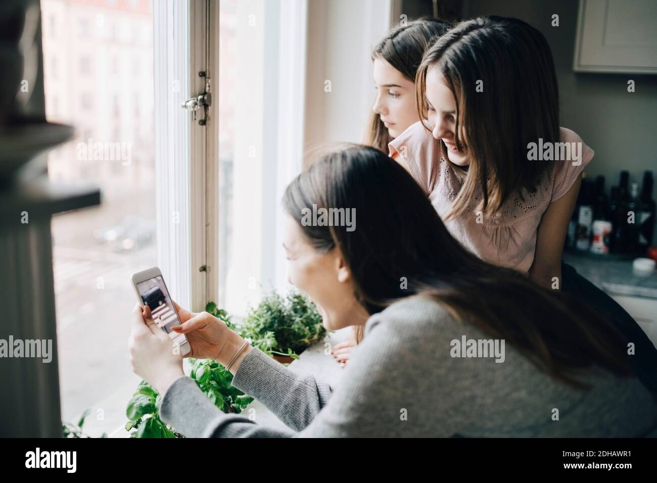 Friends looking at girl photographing through smart phone from window ...