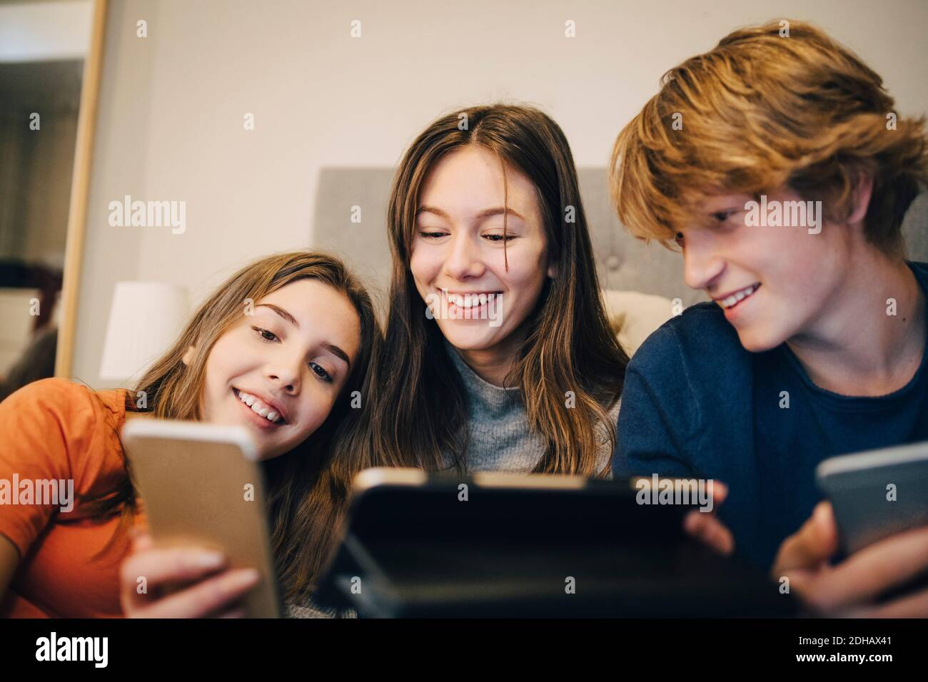 Close-up of happy friends using technology while sitting on bed at home ...