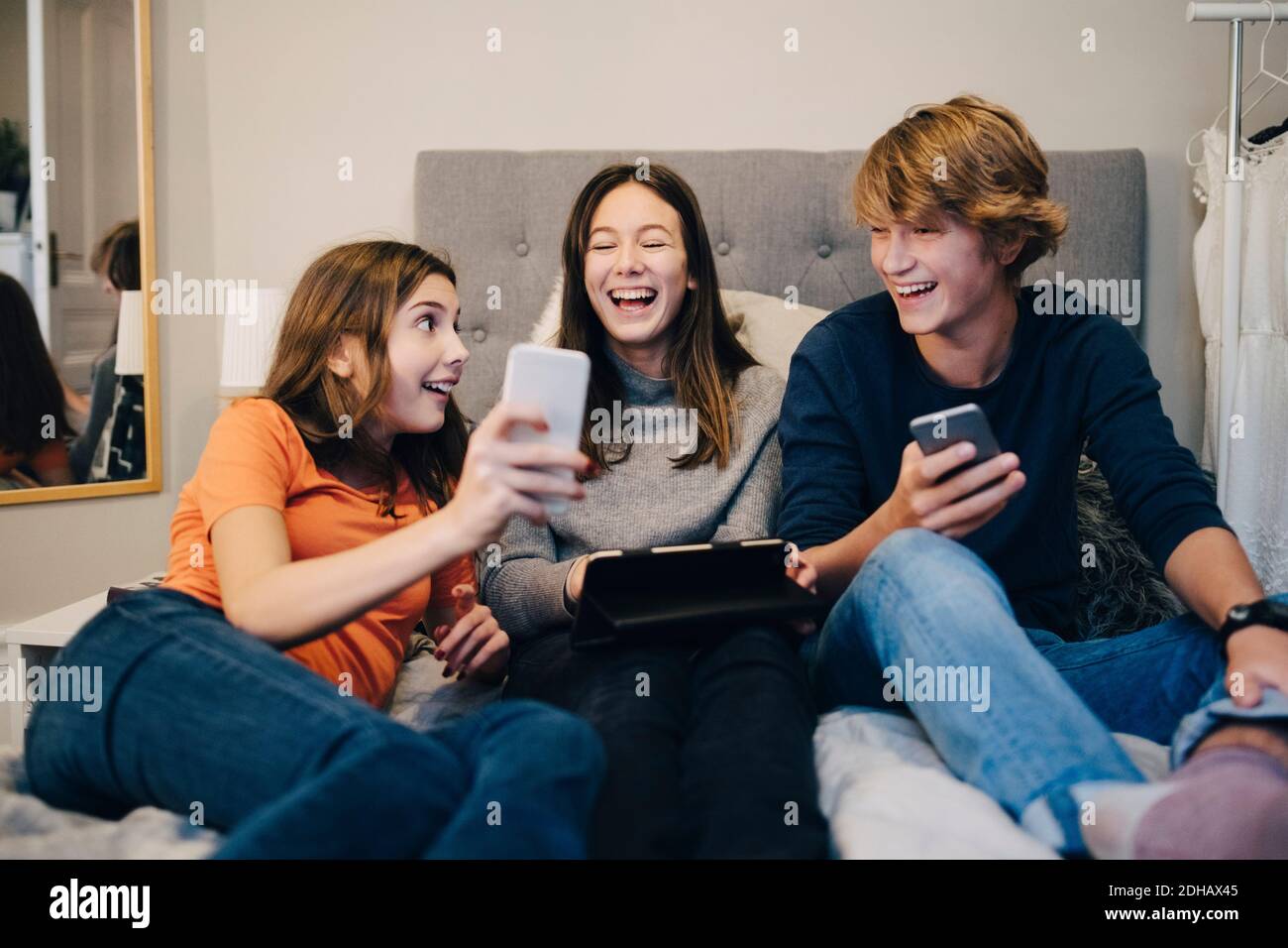Smiling friends using technology while sitting on bed at home Stock ...