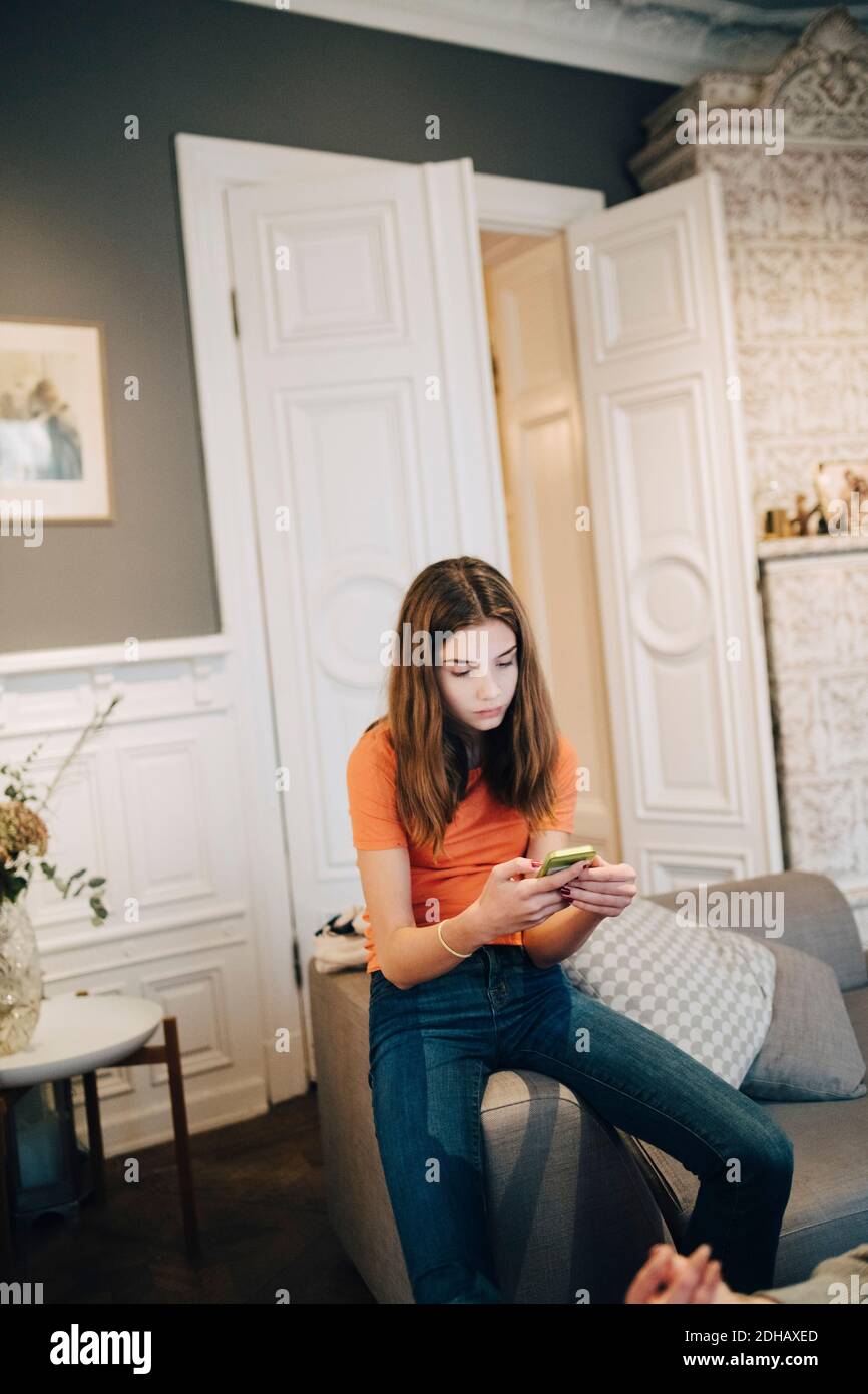 Girl using mobile phone while sitting on sofa at home Stock Photo - Alamy