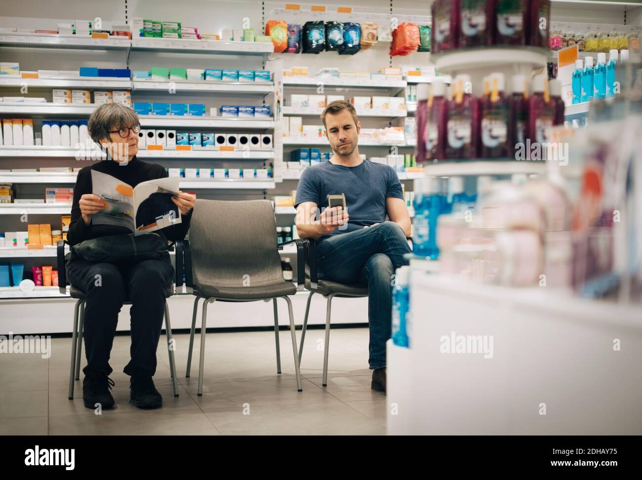 Customers sitting on chairs against medicine rack at pharmacy store ...