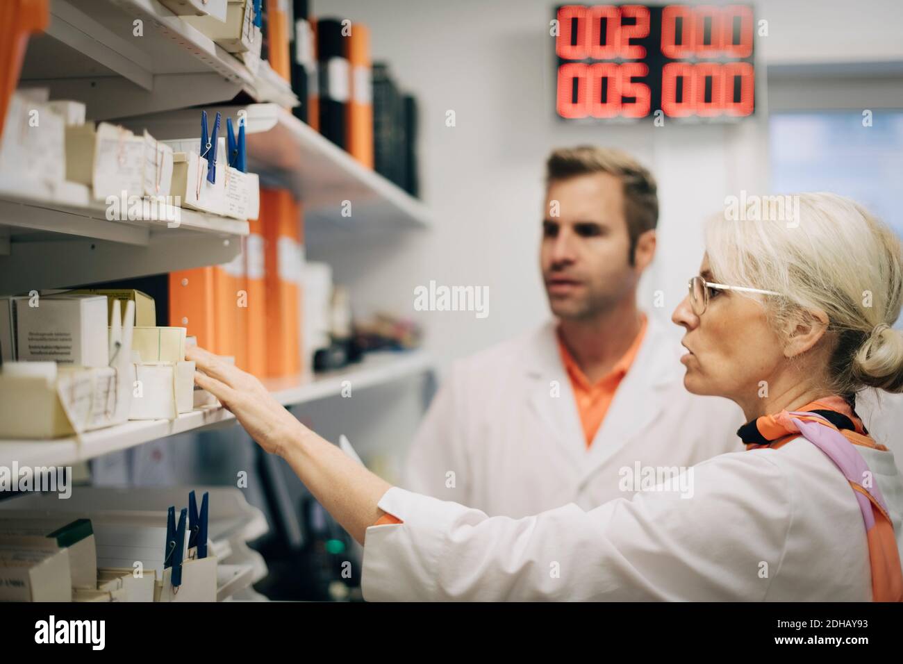 Mature medical colleagues arranging medicines on rack at pharmacy store ...