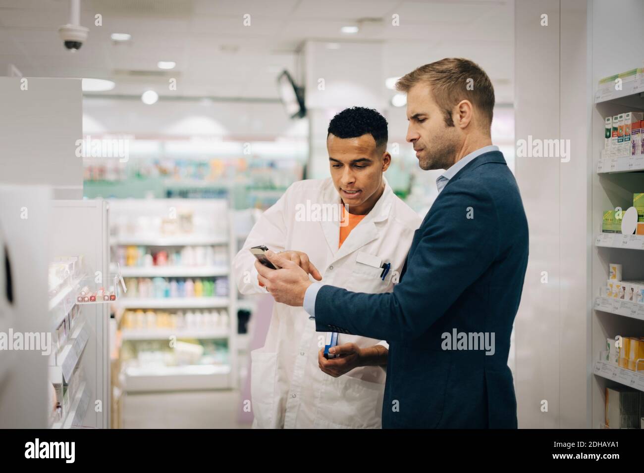 Mature customer showing mobile phone to male pharmacist standing at ...