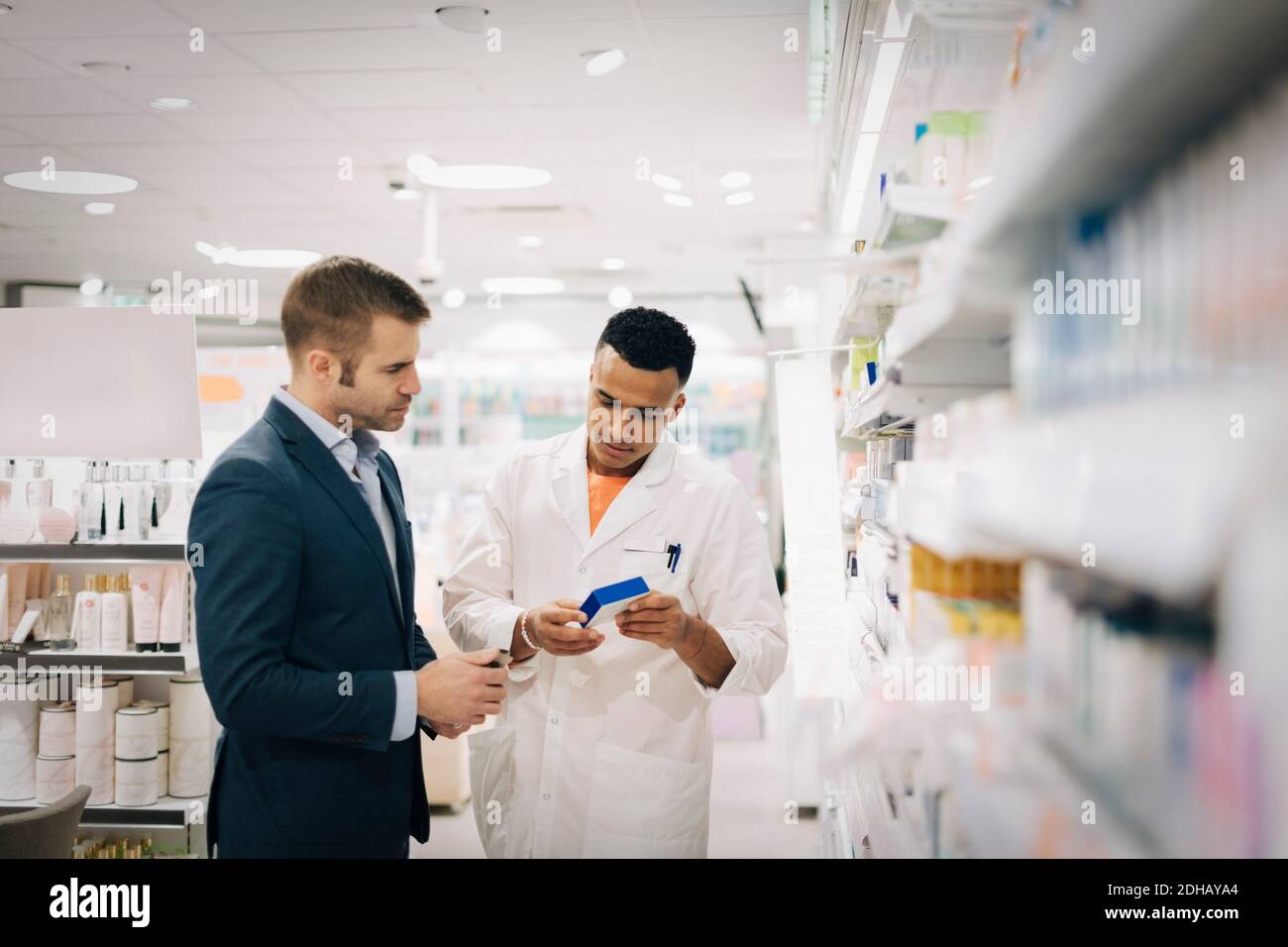 Male pharmacist showing medicine to mature customer standing by rack at ...