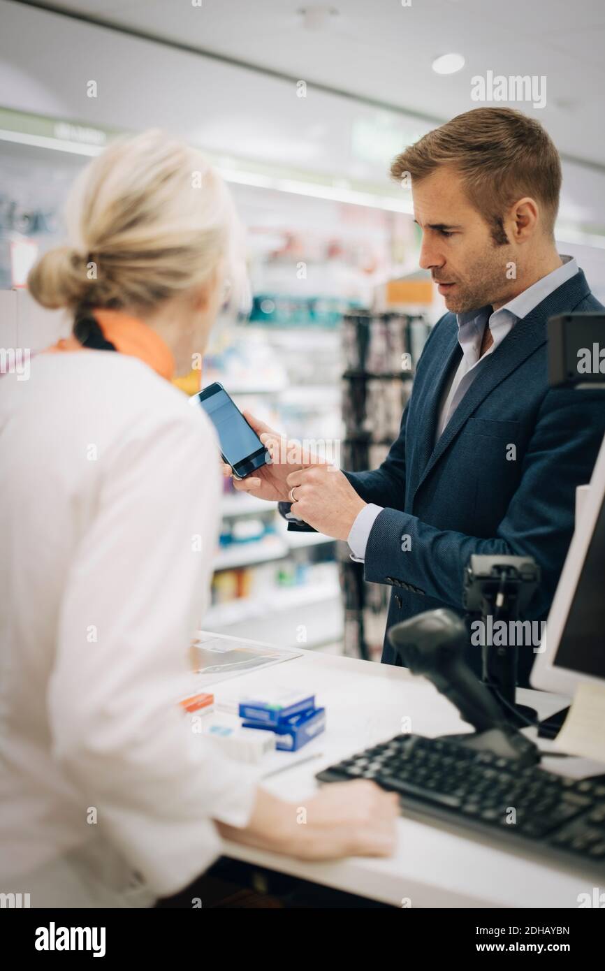 Mature man showing smart phone to female owner standing at checkout in ...