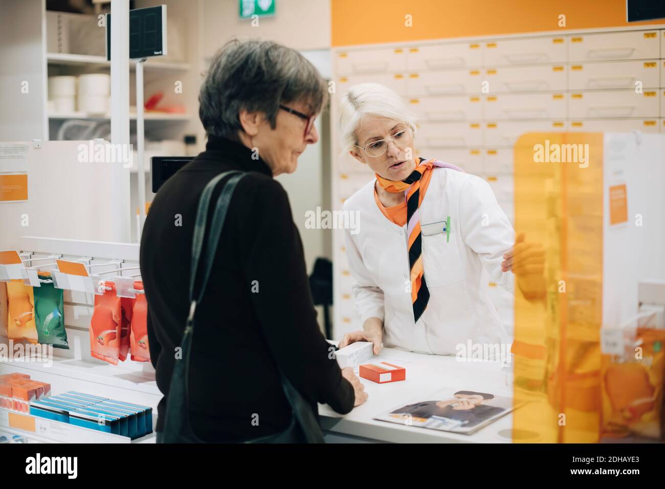 Senior customer standing with female pharmacist at checkout in medical ...