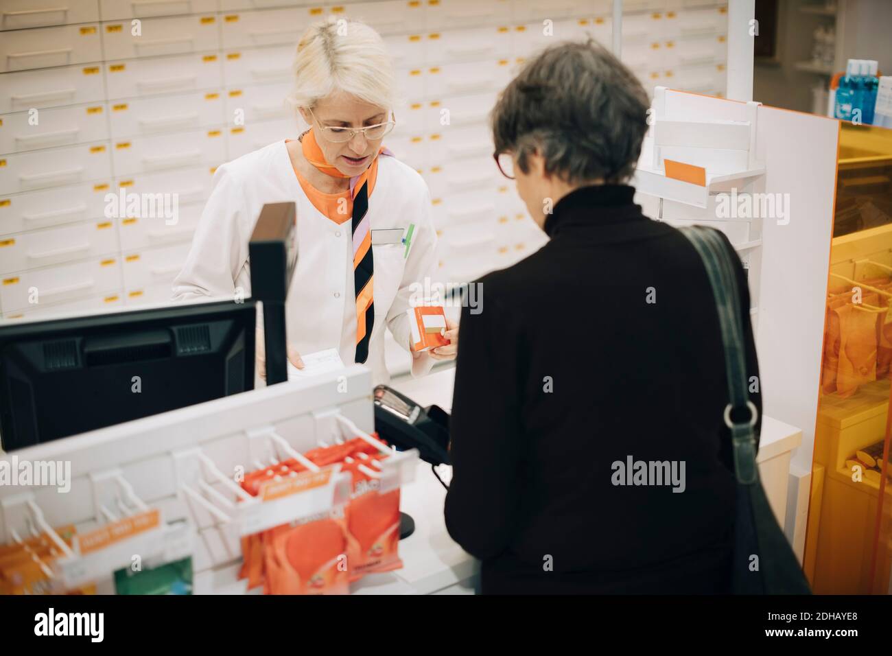 Rear view of senior customer standing with female owner at checkout in ...