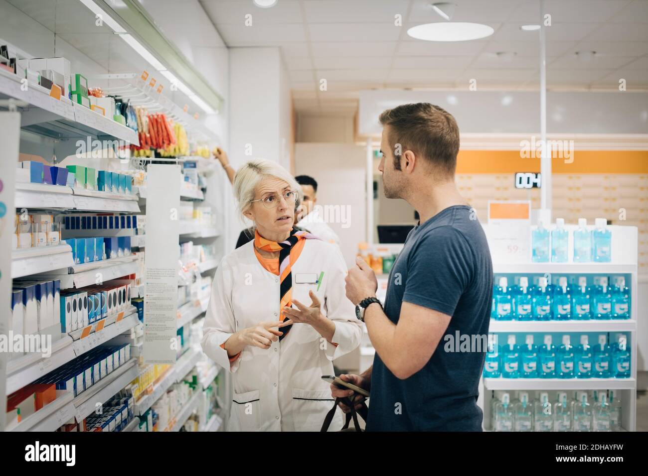 Male customer talking with female owner standing by rack at pharmacy ...