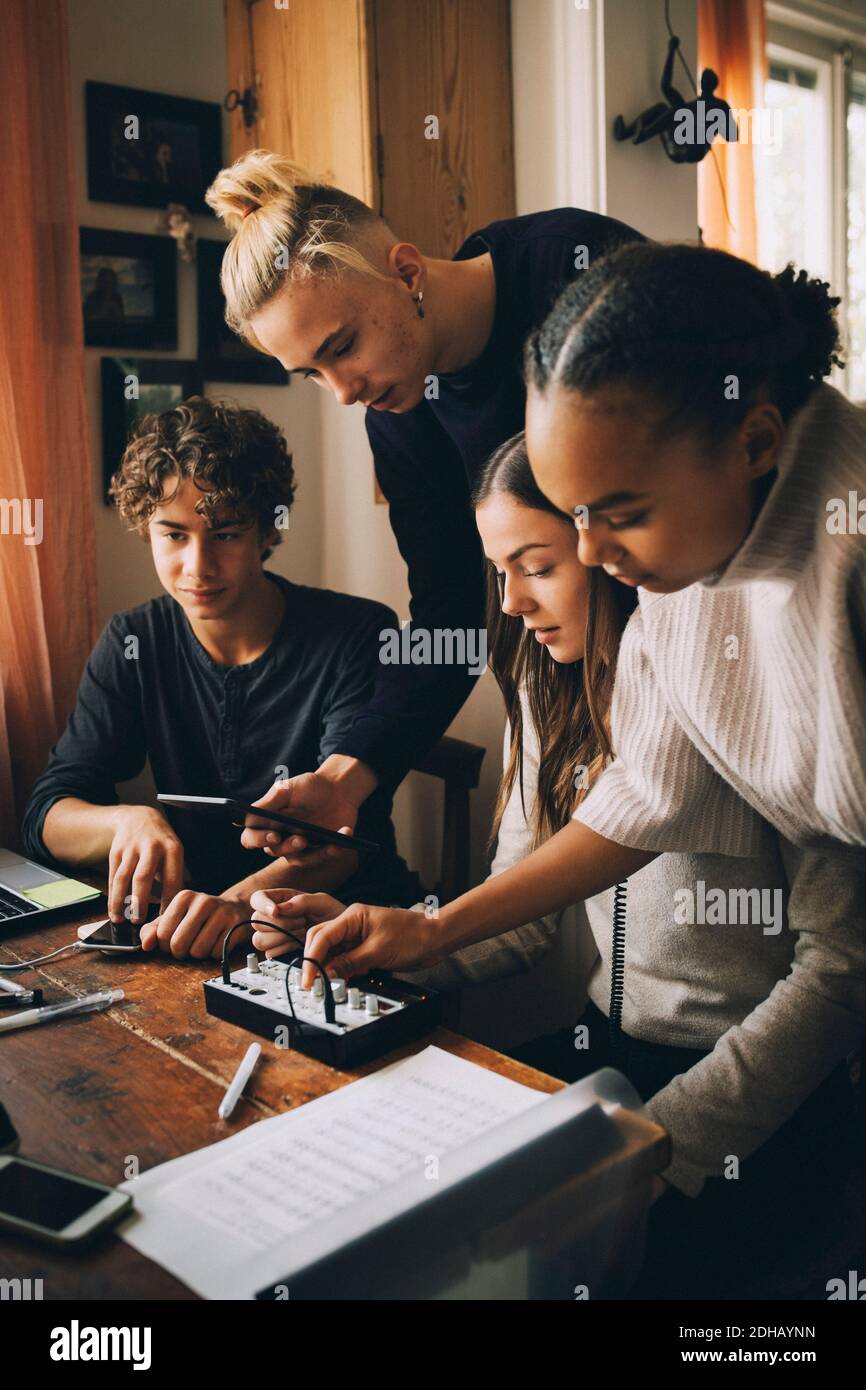 Teenage friends using audio equipment while doing homework at home ...