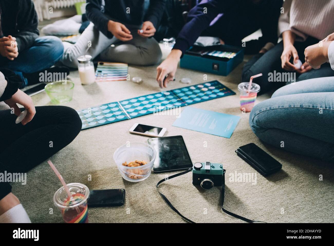 Low section of friends playing board games while having snacks on floor ...
