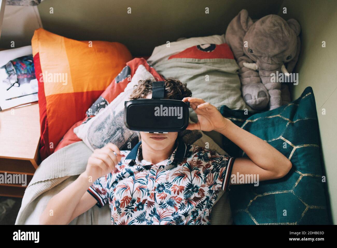 Teenage boy wearing virtual reality headset while lying on bed at home ...