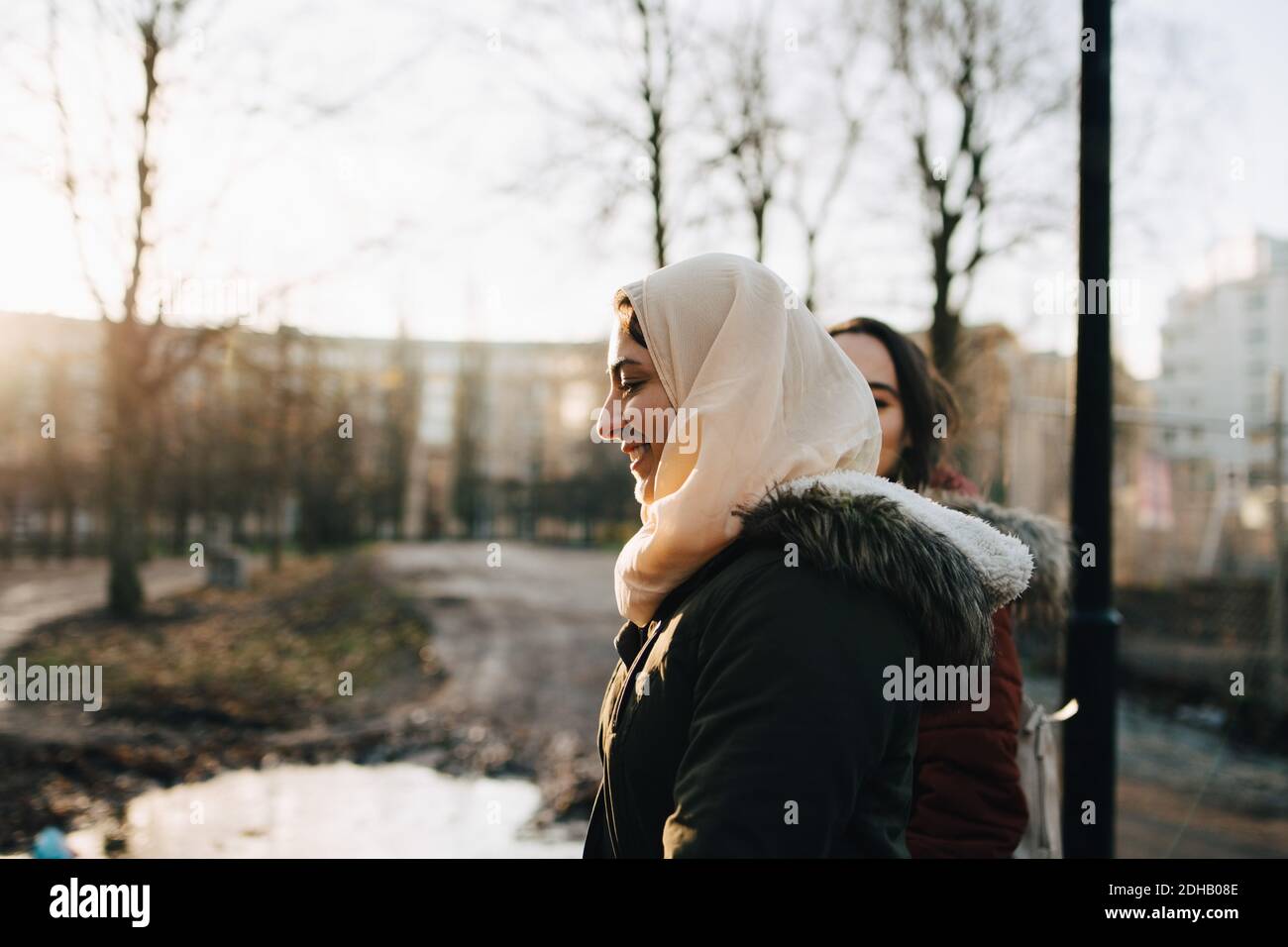 Side view of smiling young Muslim woman with female friend walking in ...