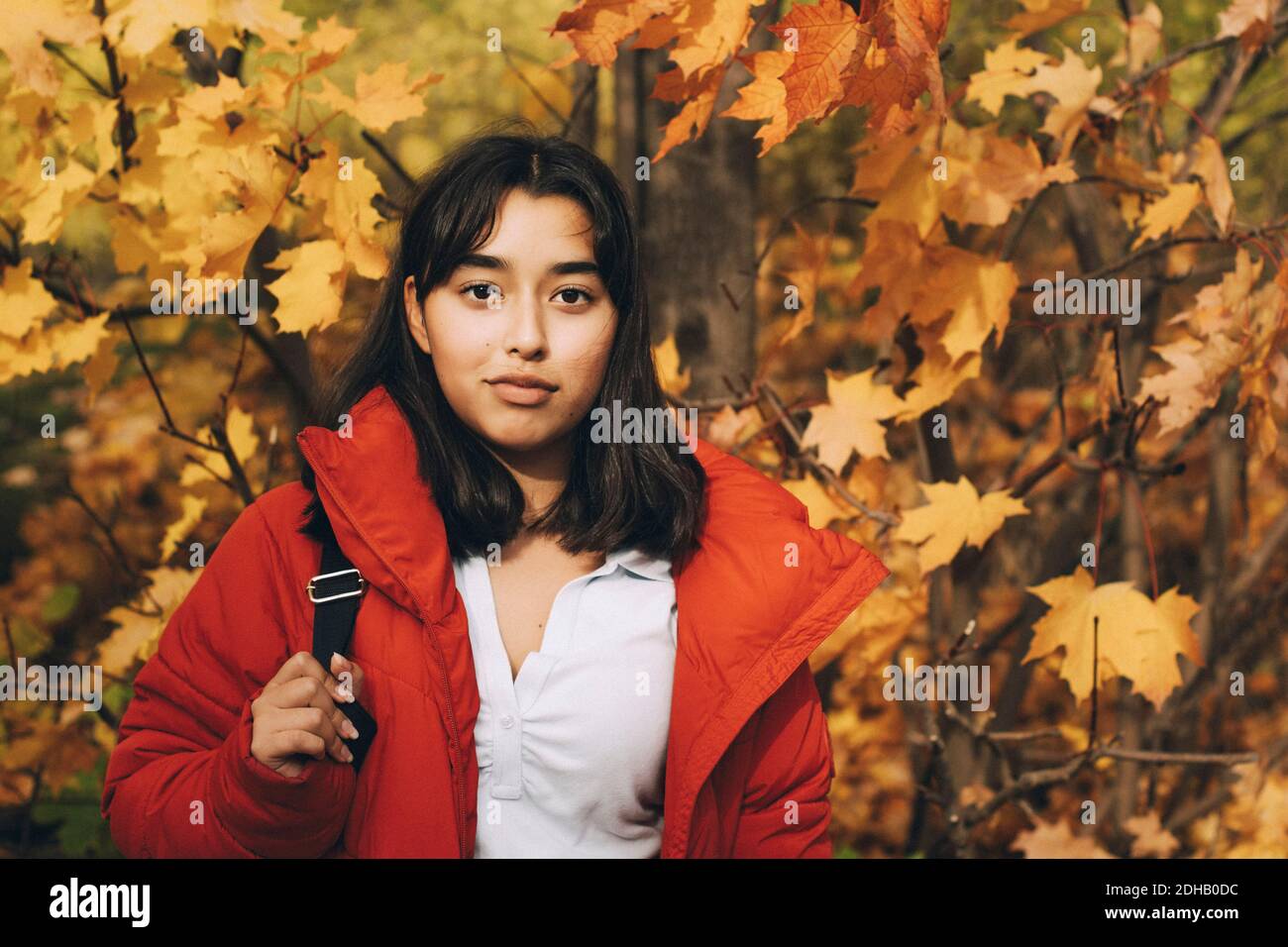 Portrait of confident teenage girl wearing red jacket standing against ...
