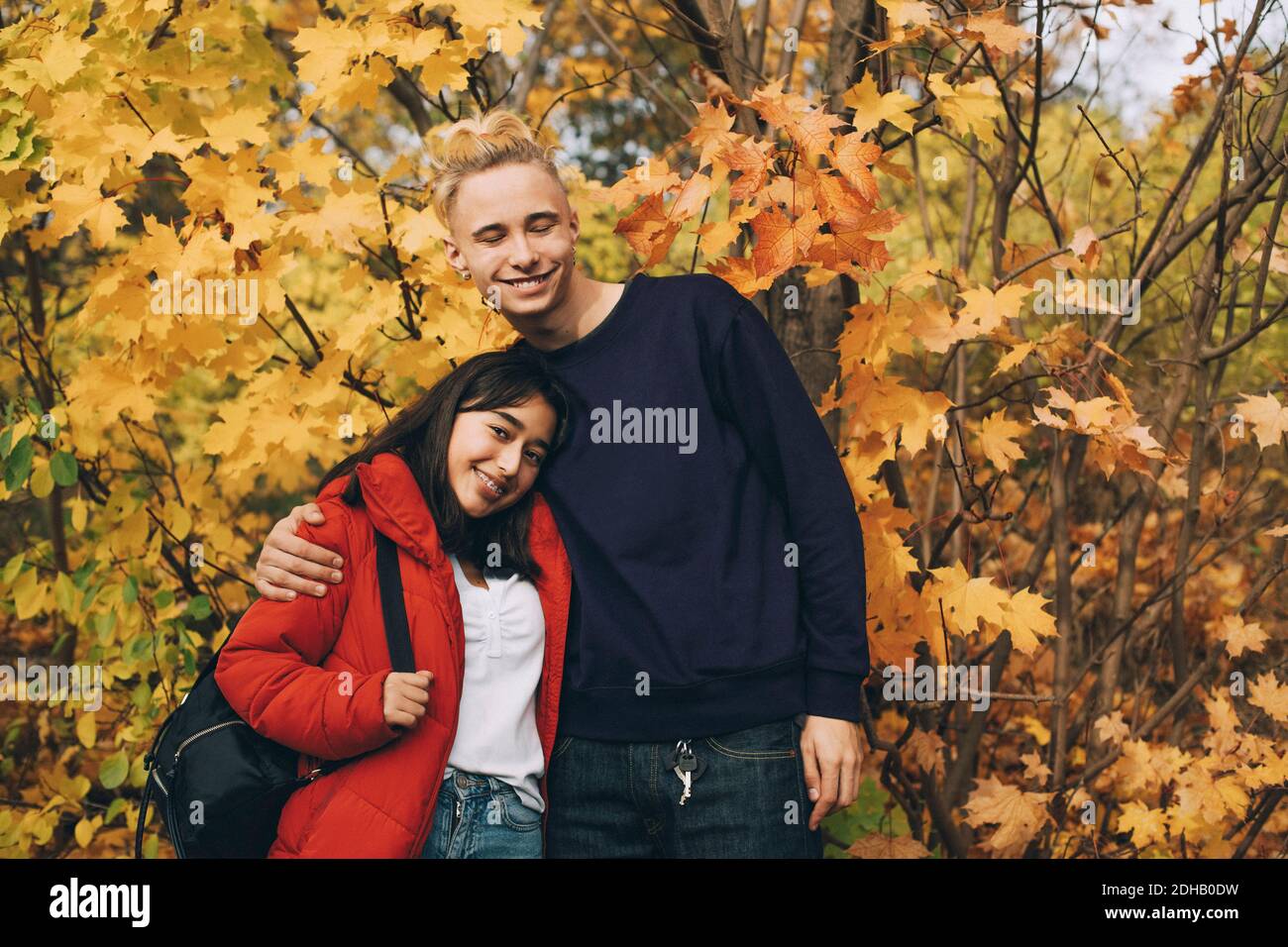 Smiling teenage friends standing against maple trees during autumn ...