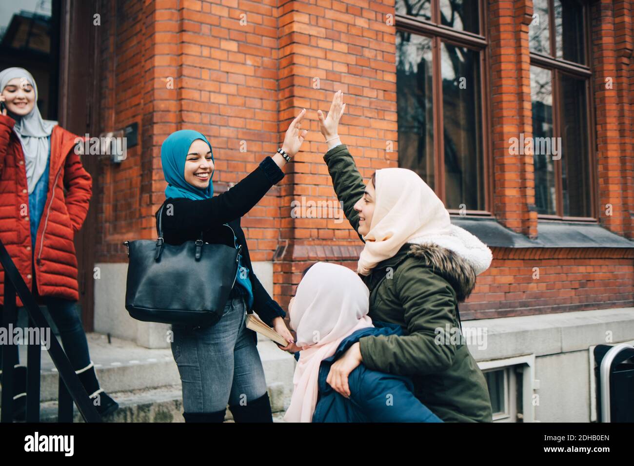 Happy female Muslim friends giving high-five against building Stock ...