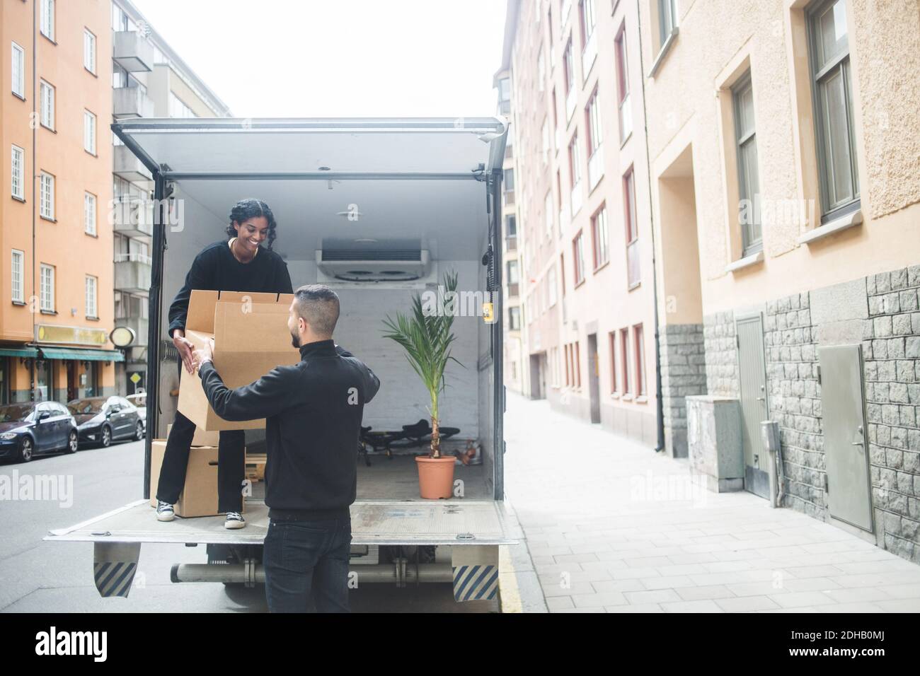 Male and female movers unloading box from truck on street in city Stock ...