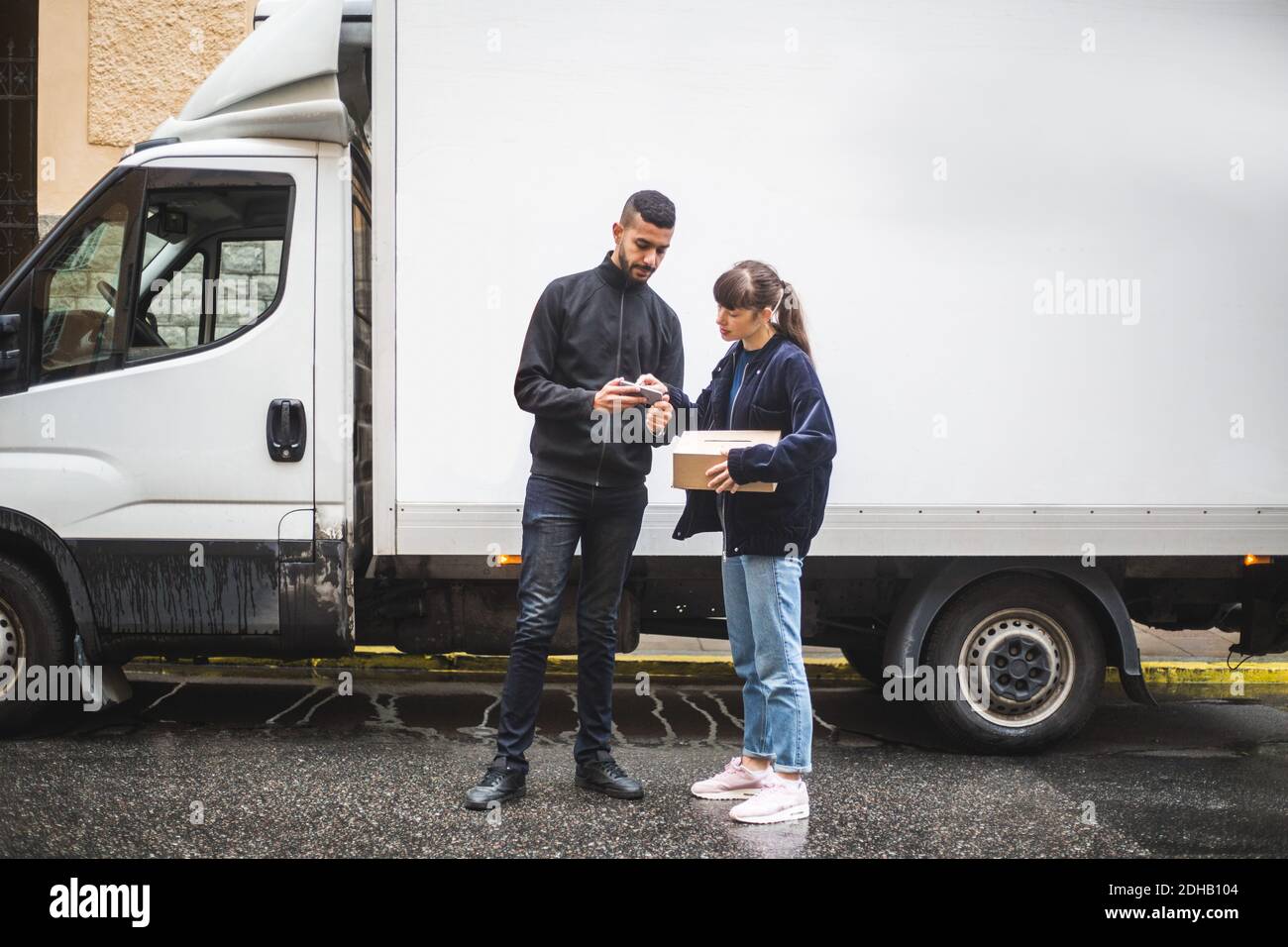 Young woman signing on smart phone while receiving package from male ...