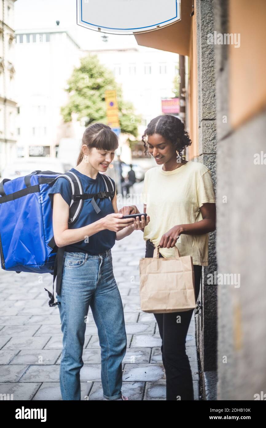 Smiling delivery woman taking sign from female customer while ...