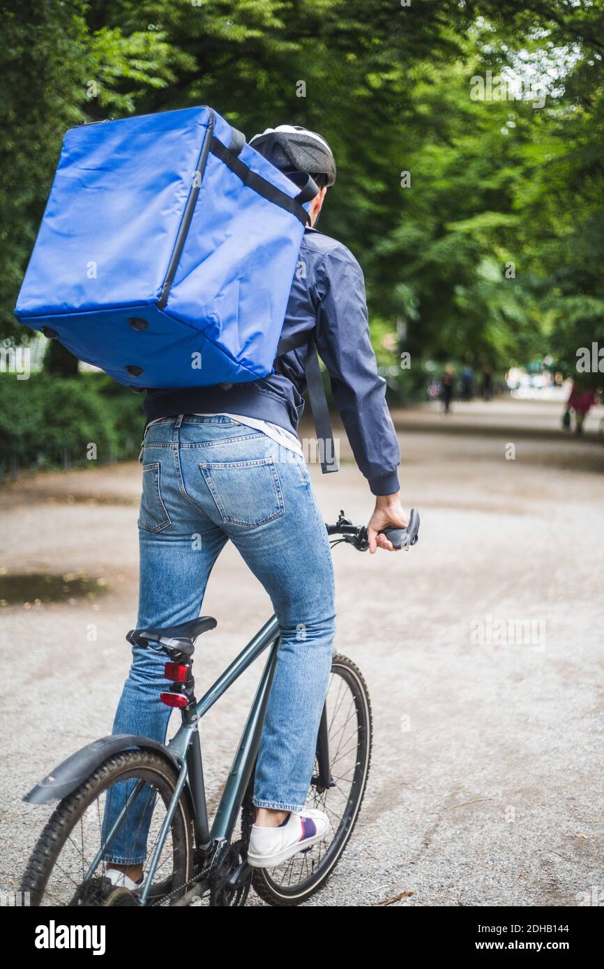Rear view of food delivery man riding bicycle on street in city Stock ...