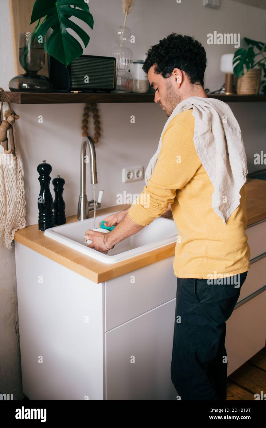 Side view of mid adult man washing utensil at sink in kitchen Stock ...