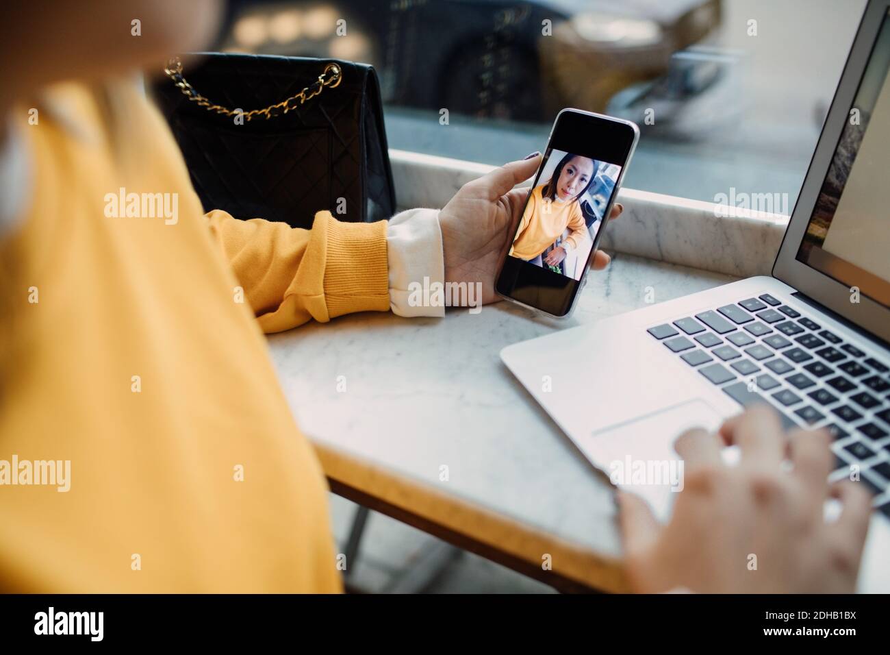 Midsection of female freelancer holding smart phone using laptop at ...