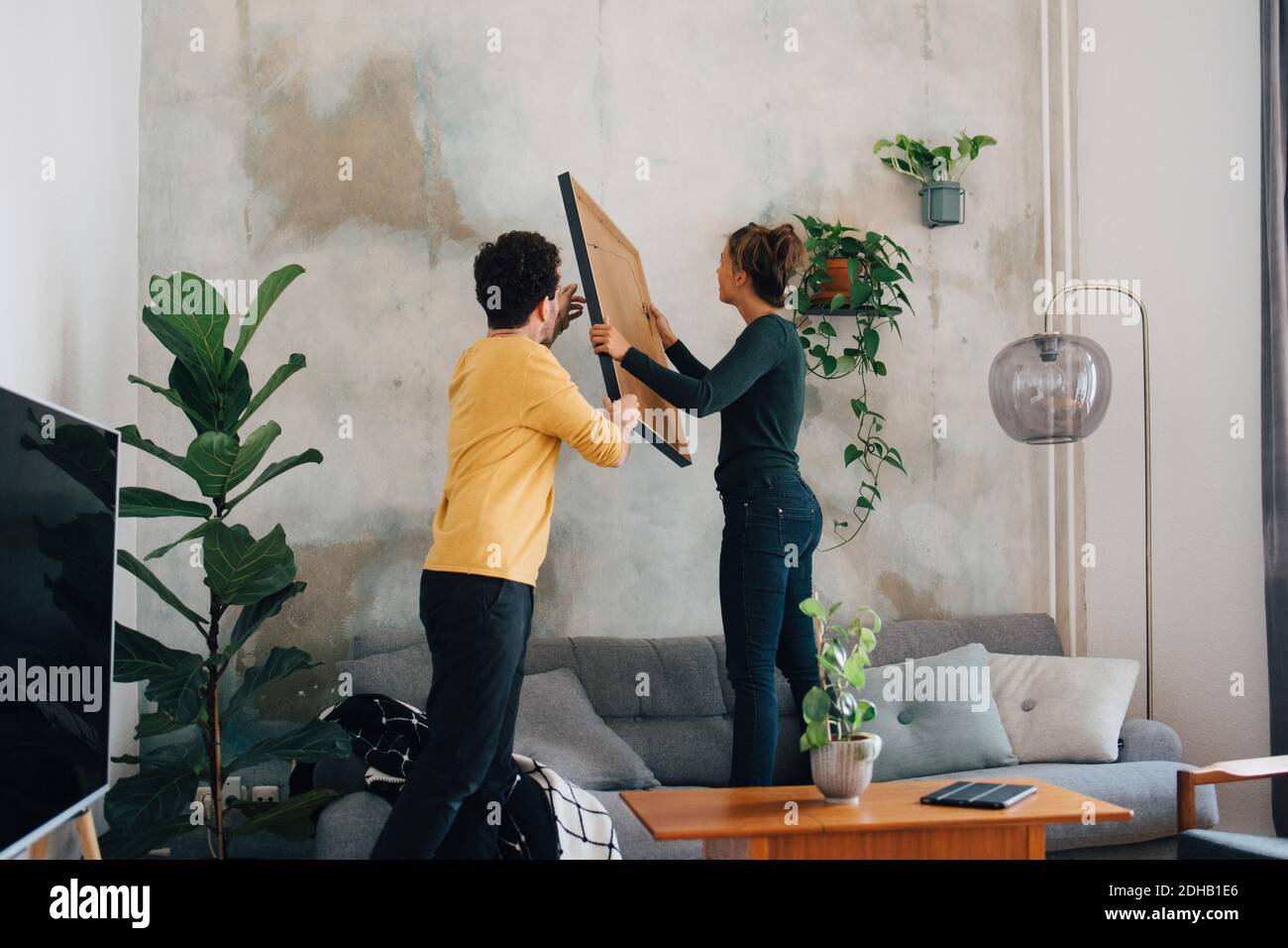 Mid adult man passing picture frame to girlfriend against wall in ...