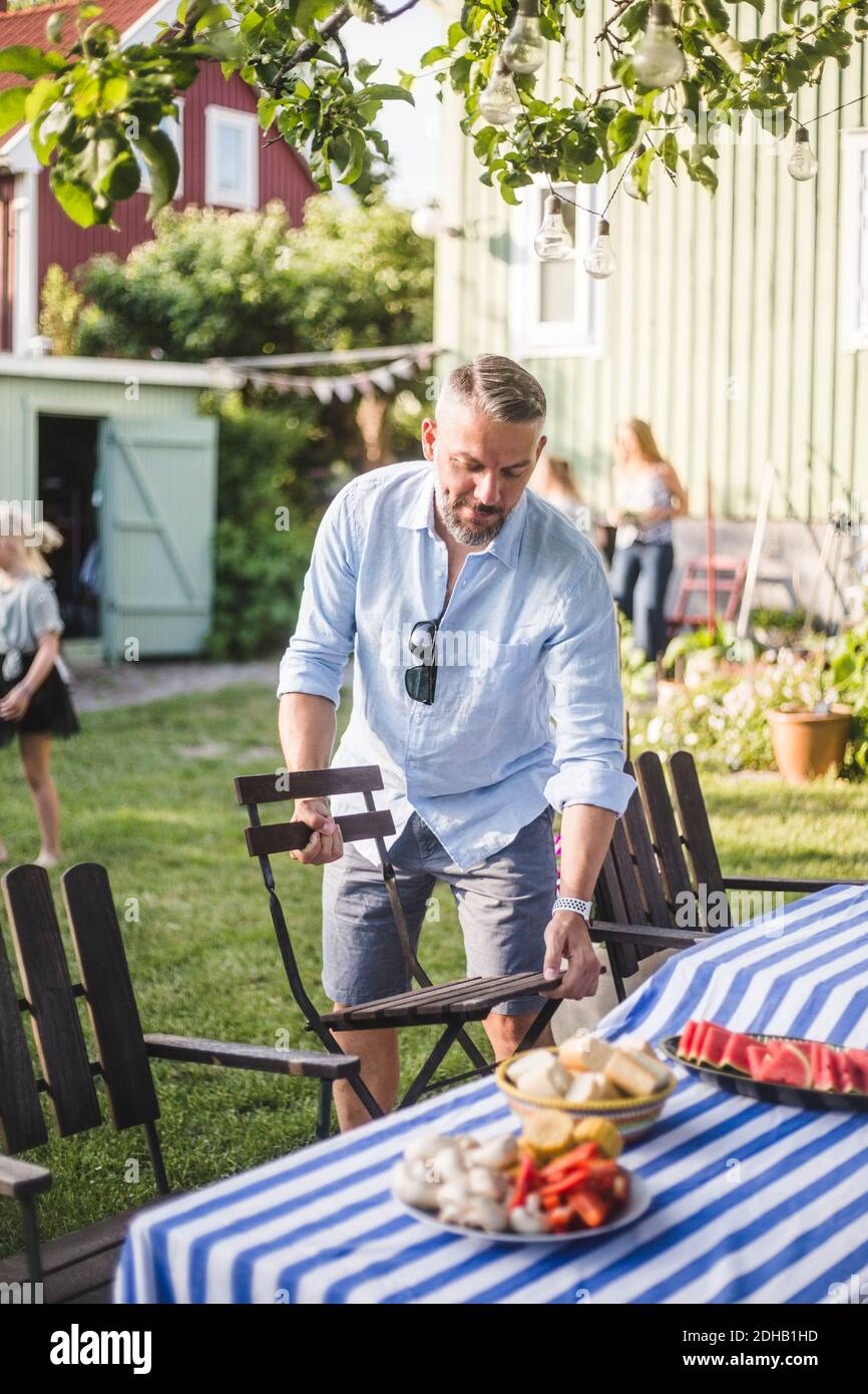 Mature man arranging chairs by dining table for garden party in ...