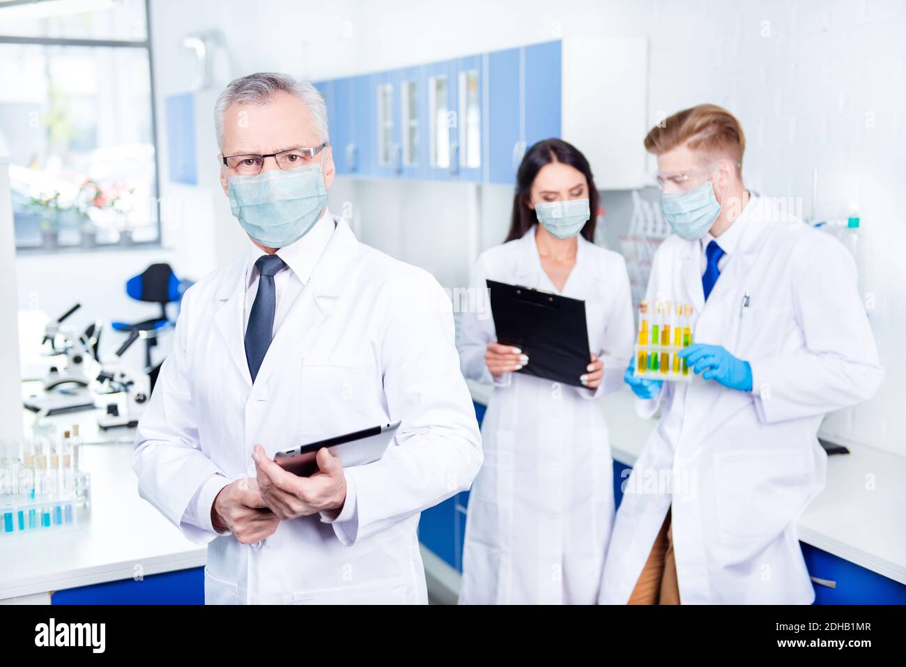 Portrait of professor in lab coat and glasses holding tablet making ...