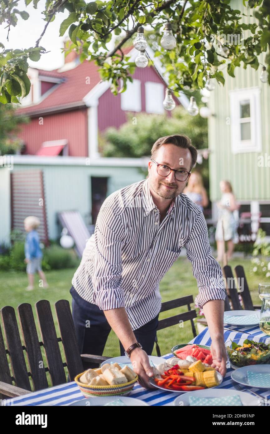 Portrait of mature man placing food plate on table in backyard while ...