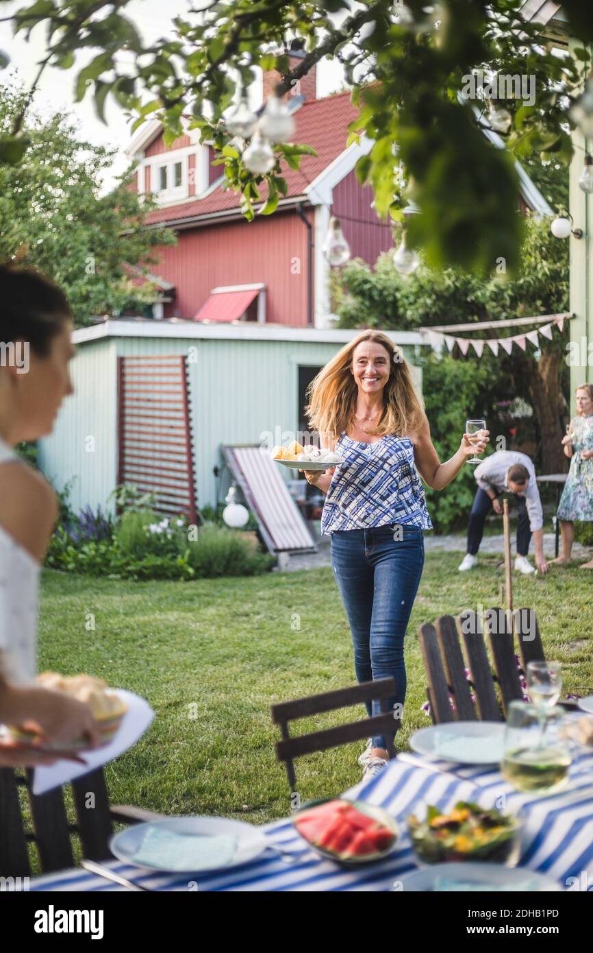 Happy woman with food plate walking towards table at garden party in ...