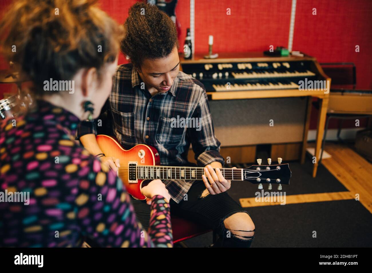 Woman sitting with friend playing guitars while practicing at recording ...