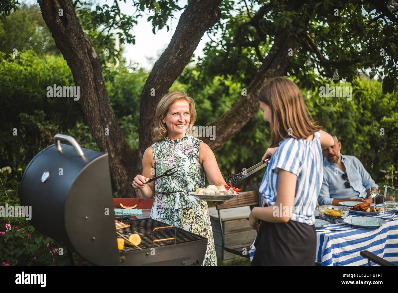 Smiling mother looking at daughter assisting in preparing food at ...