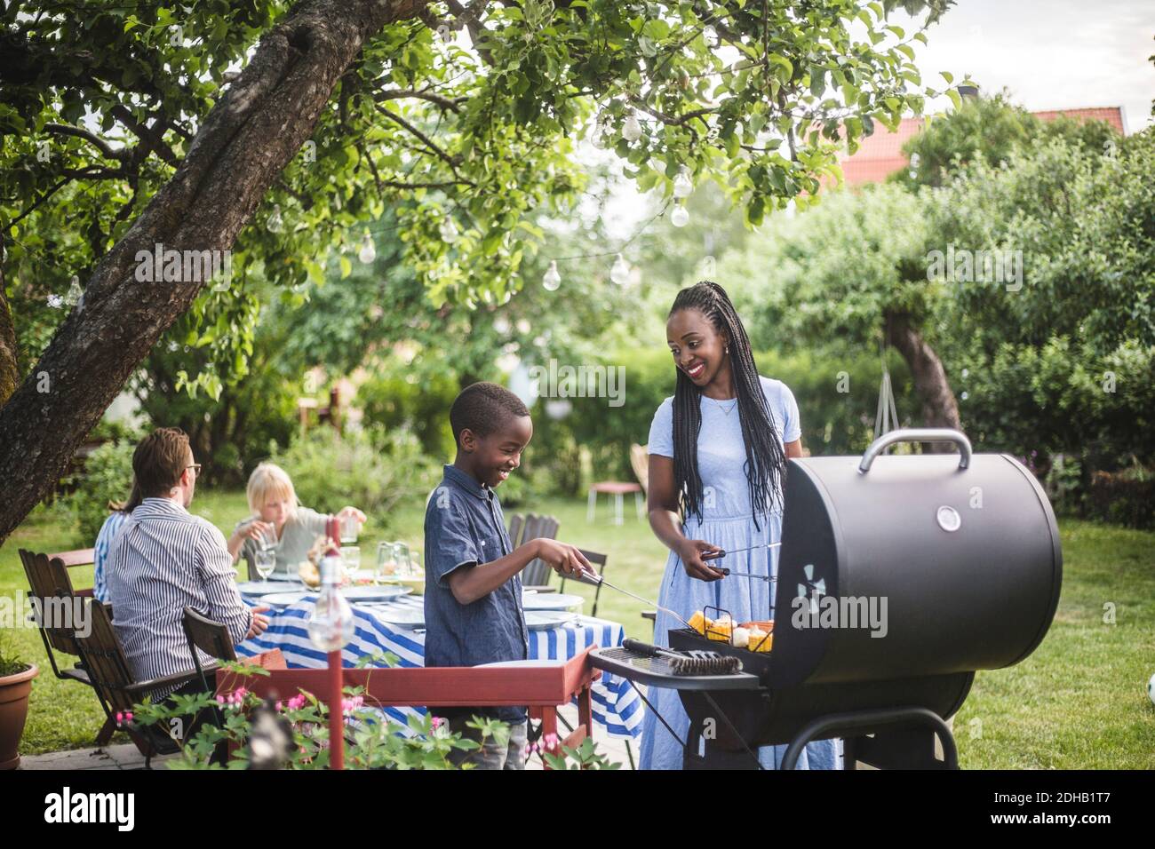 Mother and son preparing food on barbecue grill in yard during weekend ...