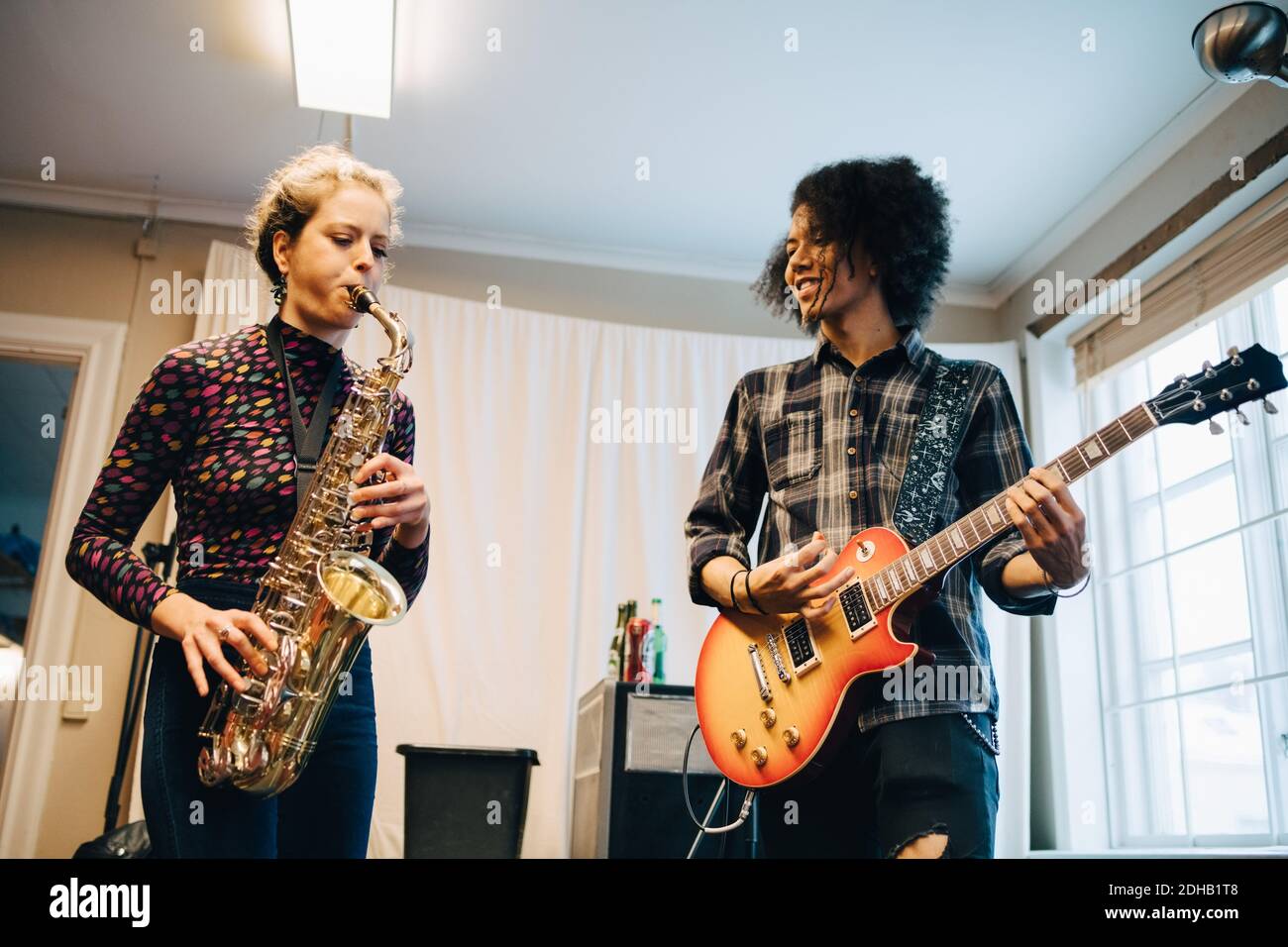 Friends playing saxophone and guitar while practicing at recording ...