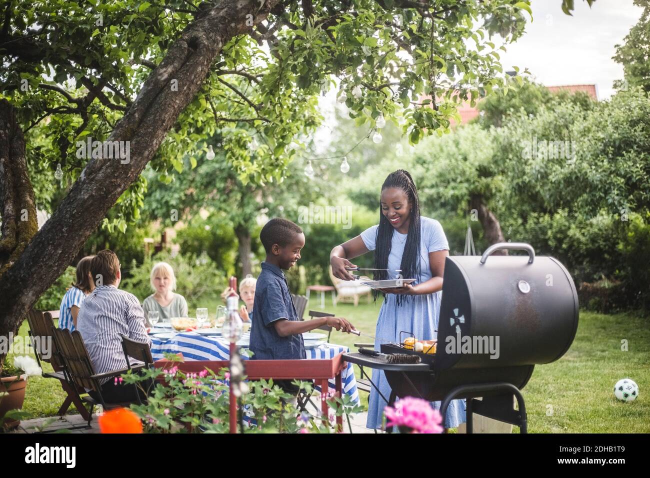 Smiling mother and son preparing food on barbecue grill together during ...