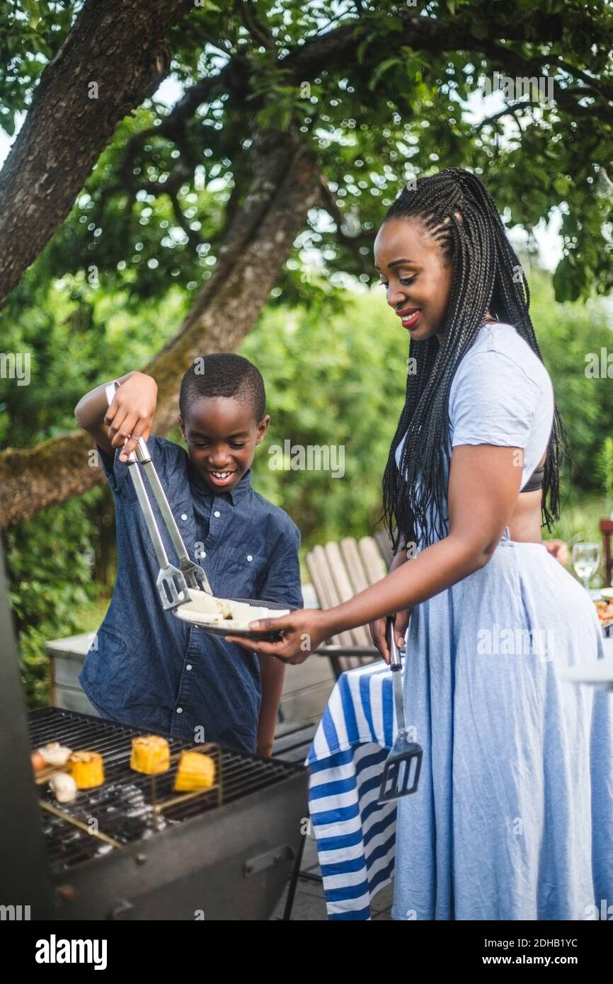 Smiling son assisting mother in preparing food at barbecue grill during ...