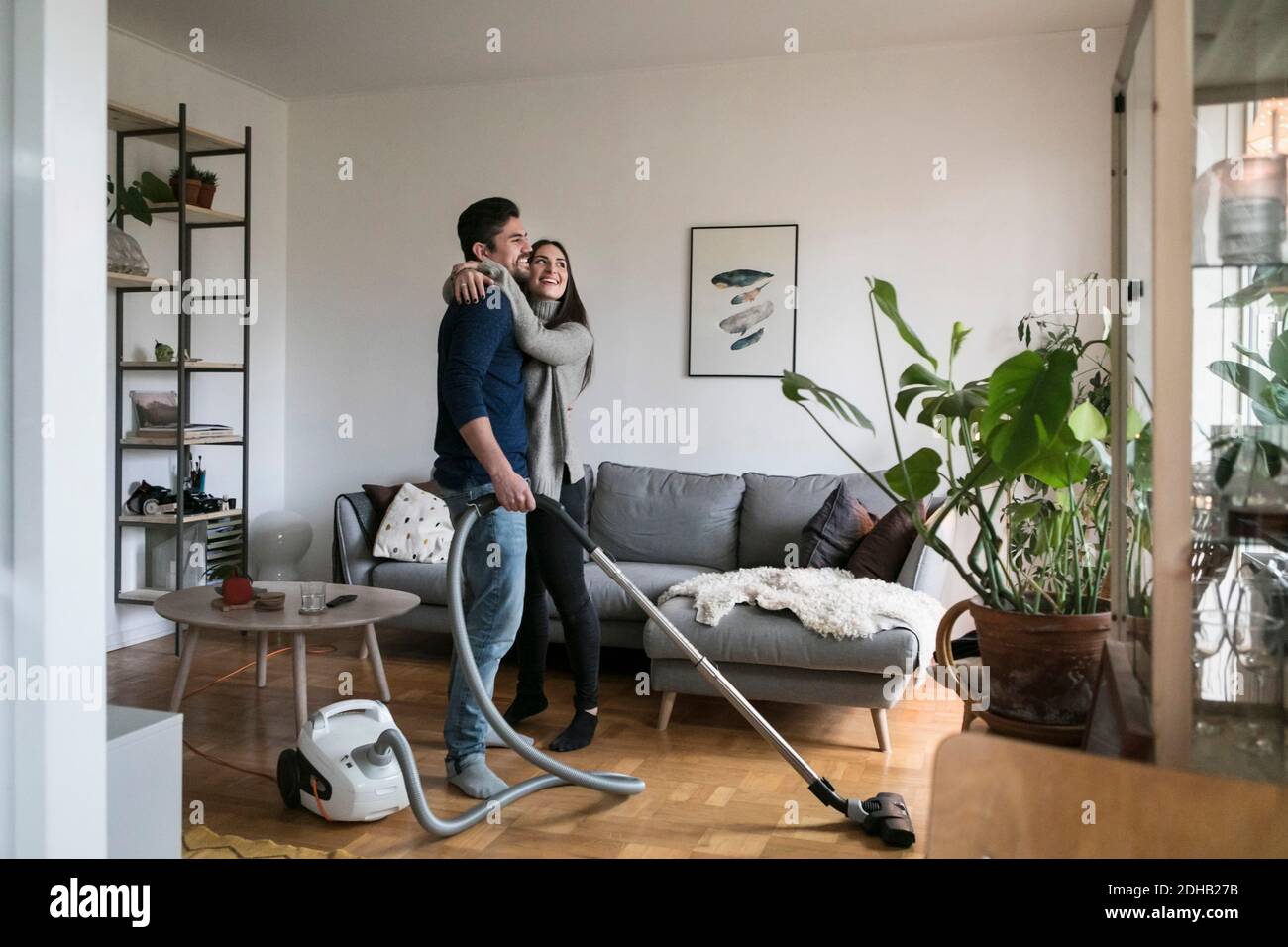 Happy couple embracing while cleaning living room at home Stock Photo ...