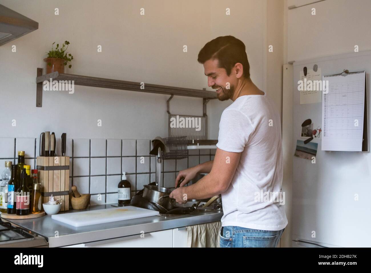 Smiling man washing utensils while standing by sink at kitchen Stock ...
