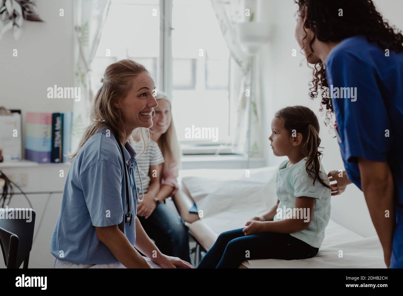 Cheerful pediatrician talking to nurse while examining girl in medical ... Cheerful pediatrician talking to nurse while examining girl in medical ...