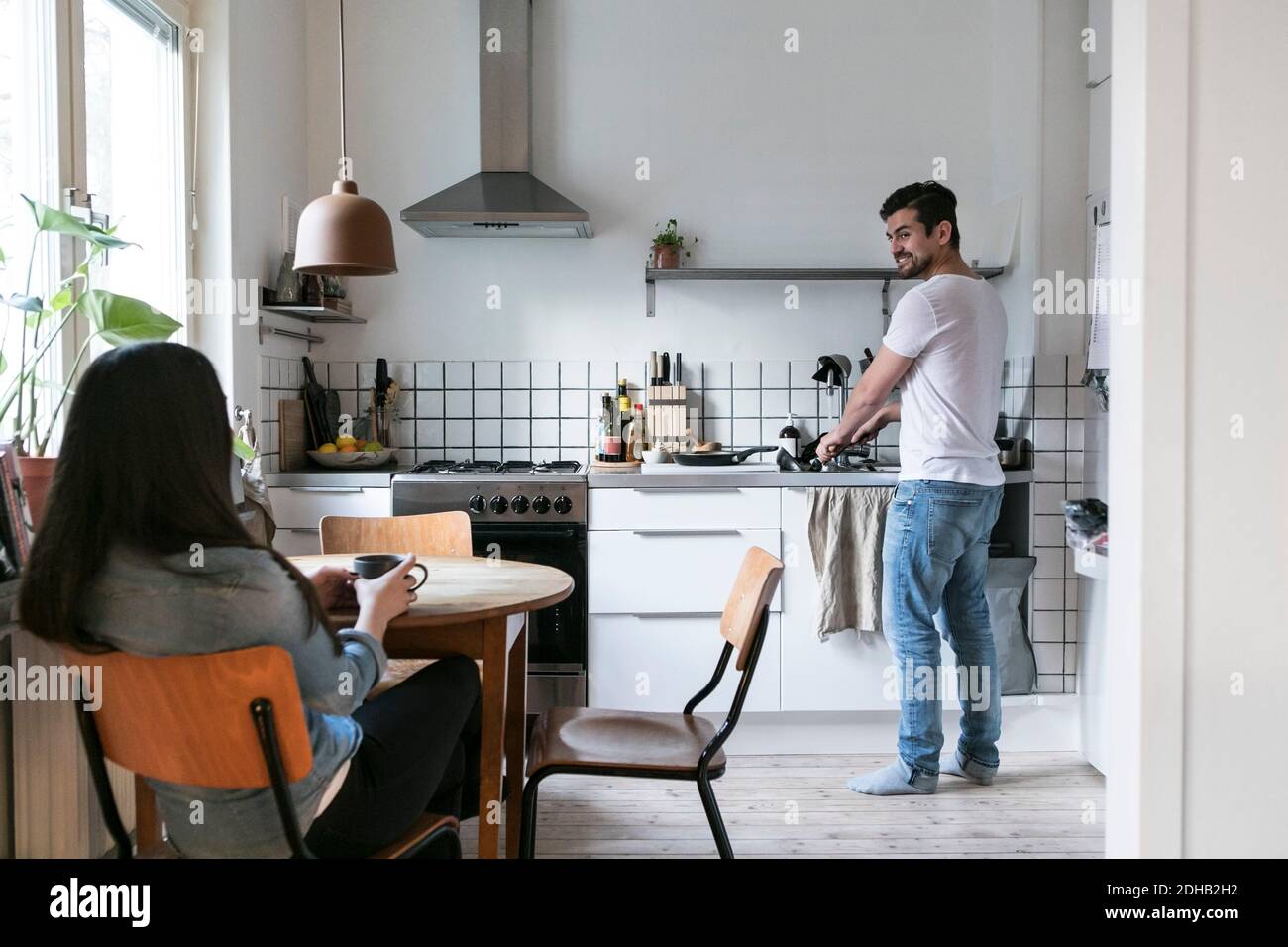 Smiling man washing utensils while woman having drink at table in ...