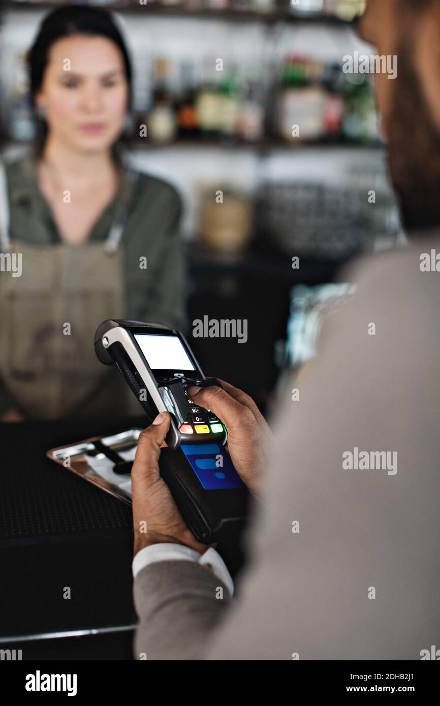 Customer using credit card reader to pay female waiter at checkout ...