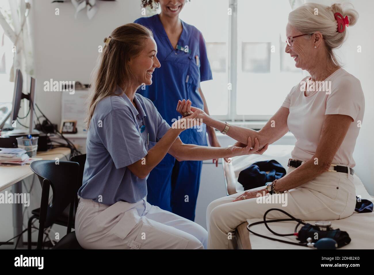 Smiling female doctor examining hand of senior patient in medical room ...